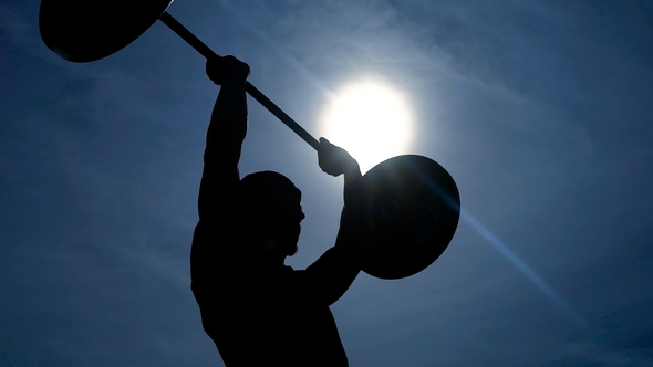 Strong Man Is Lifting a Barbell Over His Head Standing Outdoor in Sunny ...
