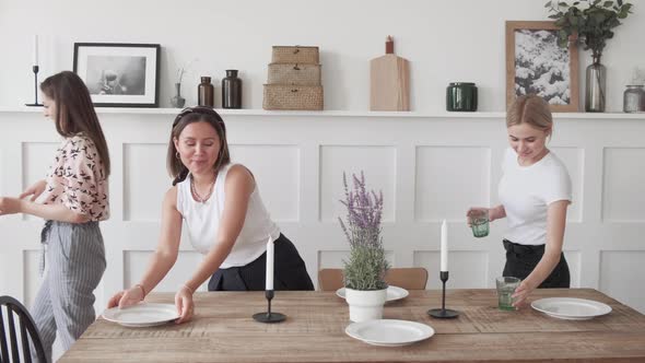 Three women are standing in the kitchen laying out plates for a joint ...