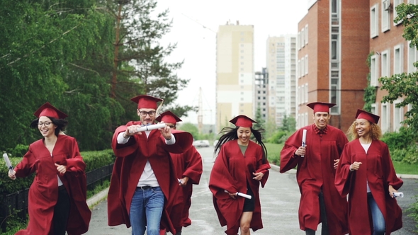 Excited Graduating Students Running Along Road on Campus Holding ...