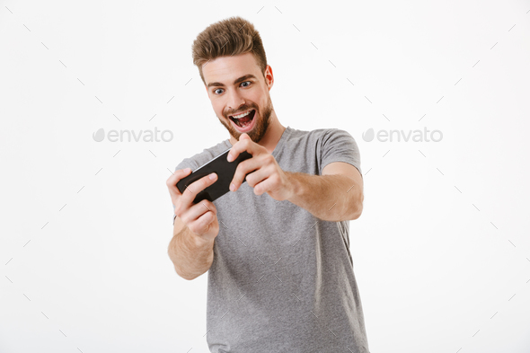Excited young man play games by mobile phone. Stock Photo by vadymvdrobot