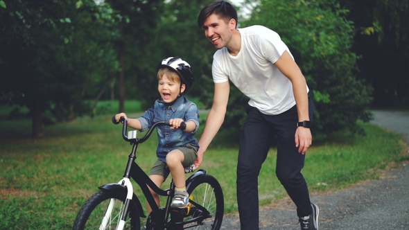 Laughing Child Cycling in Park with Careful Father Who Is Teaching Him ...