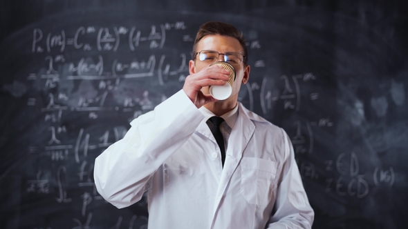 Scientist Man in White Work Robe Near Chalk Board with Equations Drinks ...
