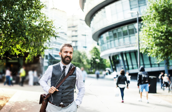 Hipster businessman with earphones walking on the street in London ...