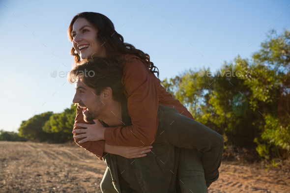Man giving woman piggyback ride on field Stock Photo by Wavebreakmedia