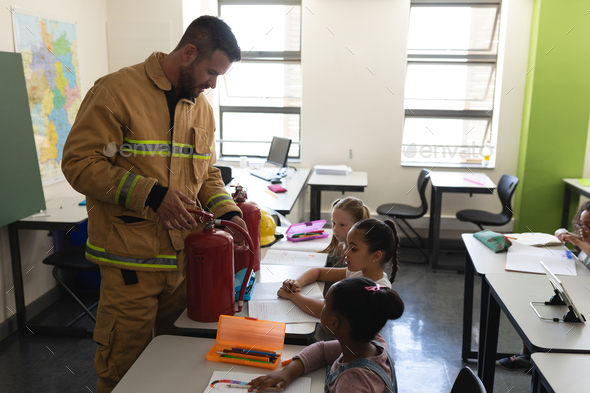 Male firefighter teaching schoolkids about fire safety in classroom of ...