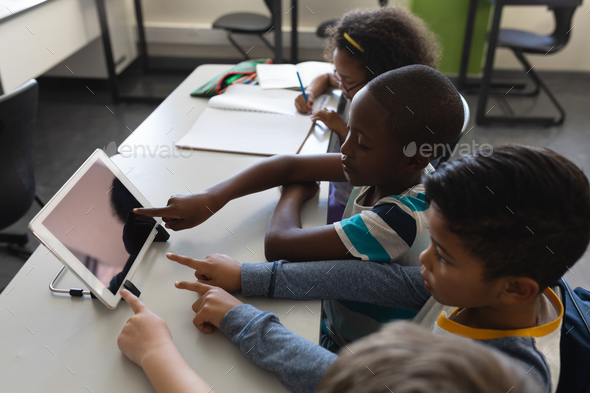 Schoolkids studying on digital tablet while sitting at desk in ...