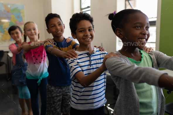 School kids standing in row with their hands on shoulder in classroom ...