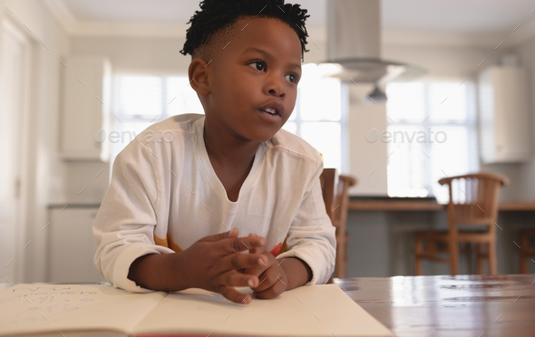 Front view of thoughtful cute African American boy doing homework at ...