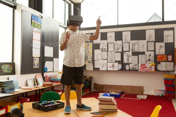 Schoolboy using virtual reality headset while standing on a desk in ...