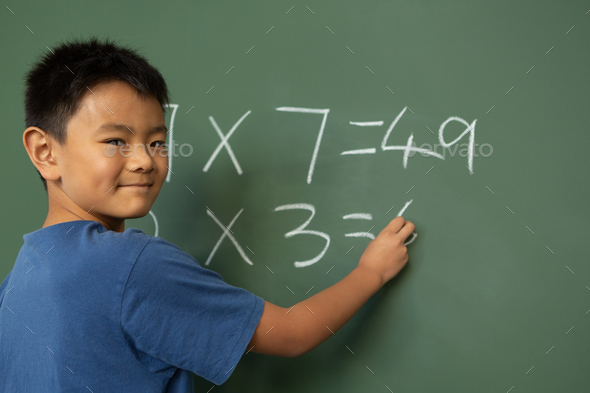 Front view of an Asian schoolboy doing math on greenboard in a ...