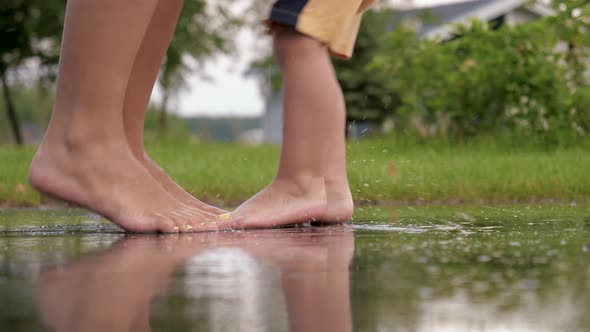 Close Up Legs Of Playful Baby And Mother Barefoot Stomping On Puddle On ...