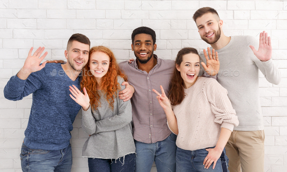 Happy friends waving hands over white wall Stock Photo by Prostock-studio
