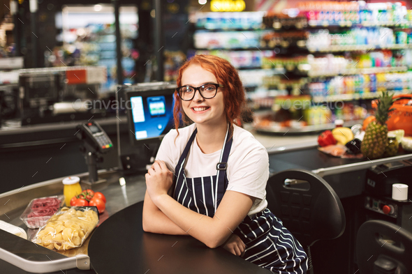 Pretty smiling cashier in eyeglasses and striped apron happily l Stock ...