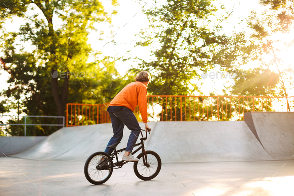 Cool young guy in orange pullover and jeans from back riding bic Stock ...