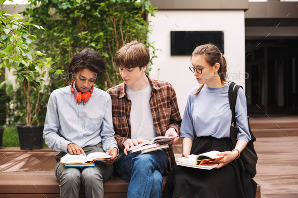 Group of students sitting on bench and thoughtfully reading books in ...