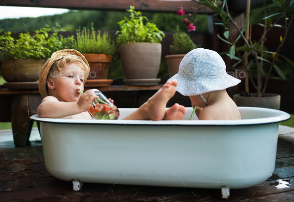 Small children with a drink sitting in bath outdoors in garden in ...