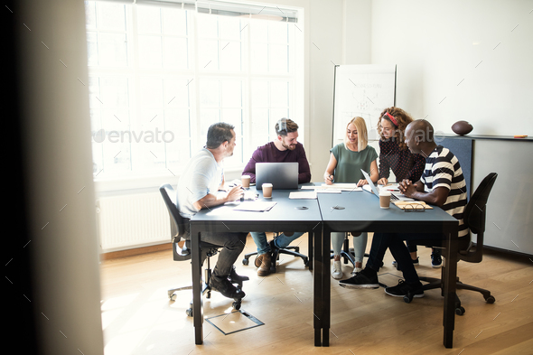 Smiling designers sitting around an office table working on project ...