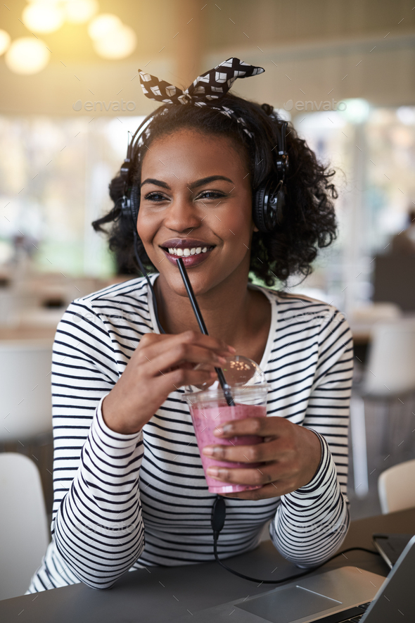 Smiling African university student sitting on campus drinking a ...