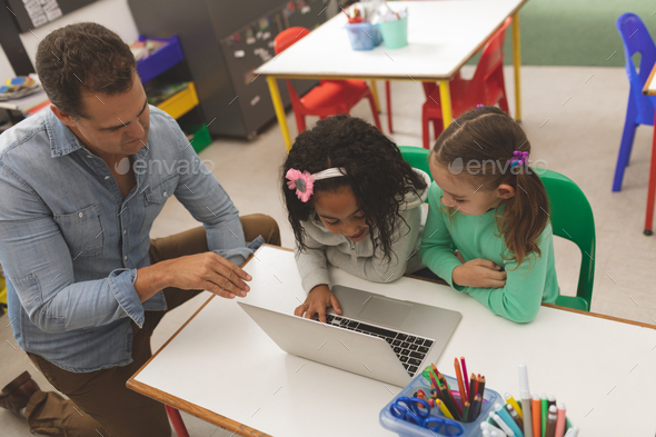 Schoolgirls working on laptop while their teacher teaching them how to ...