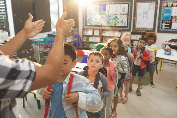 Front view of school kids standing and forming a queue in classroom at ...