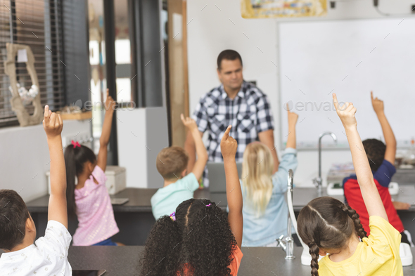 Schoolkids raising hand in classroom to answer at a question of the ...