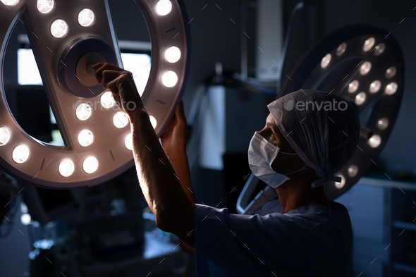 Side view of a Caucasian female surgeon fixing surgical light at ...