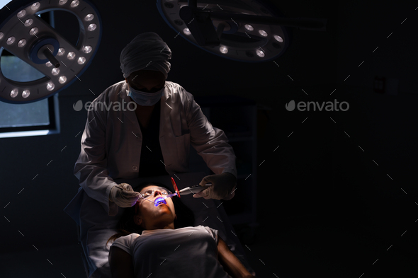 Mature female dentist examining a patient with dental curing light in ...