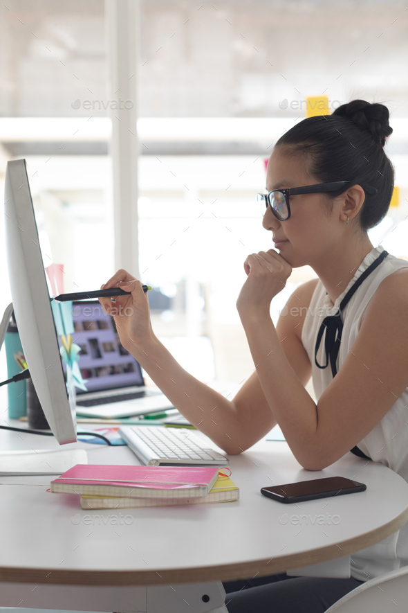 Side view of Asian female graphic designer working on computer at desk ...