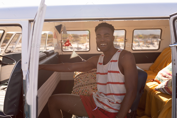 front view of happy young African-american man sitting in camper van at ...