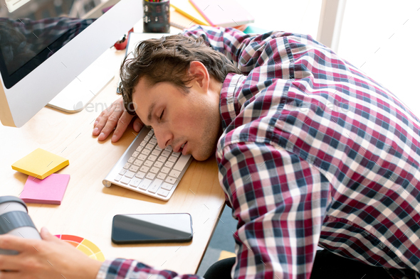 High view of tired Caucasian male graphic designer sleeping on desk in ...