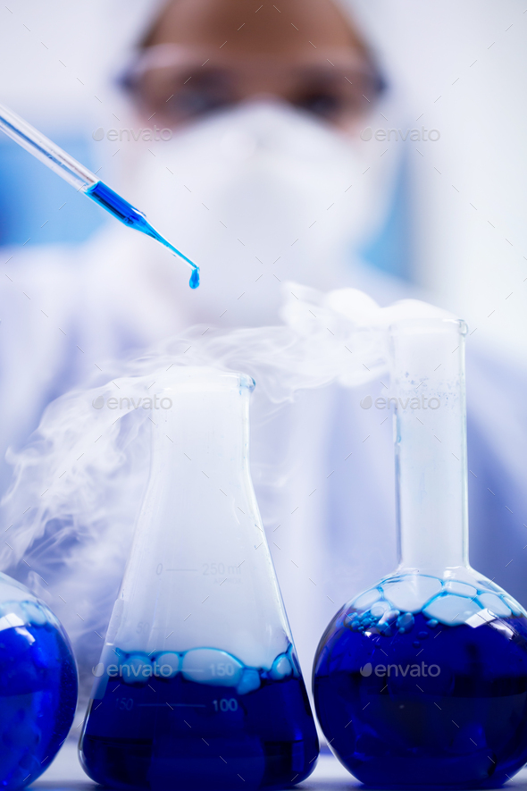 Close up of blue solution dropping from pipette in a test tube with ...