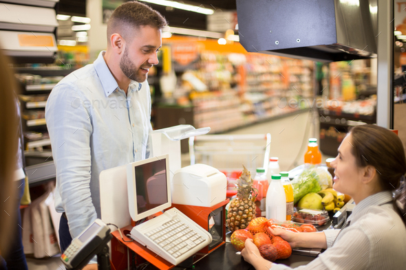 Customer Smiling to Cashier in Supermarket Stock Photo by seventyfourimages