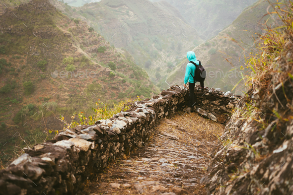 Hiker with backpack on the mountain edge cobbled path looking down the ...