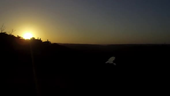 Left to right pan of the sun setting behind a hill and a river valley ...