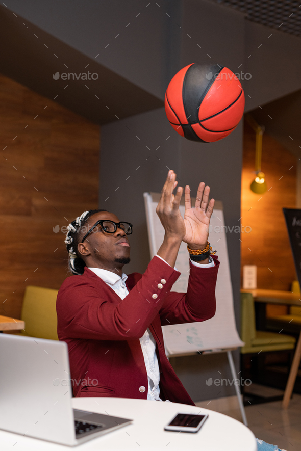 African guy throwing ball upwards while sitting by table in modern cafe ...