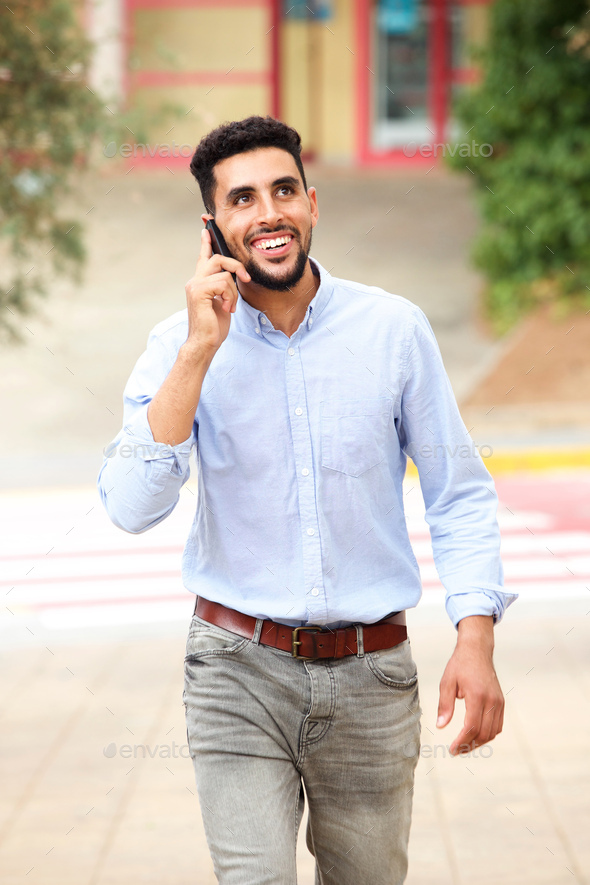 smiling young arabic man walking on the street and talking on ce Stock ...