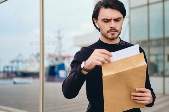 Young serious brunette man angrily opening envelope with response ...