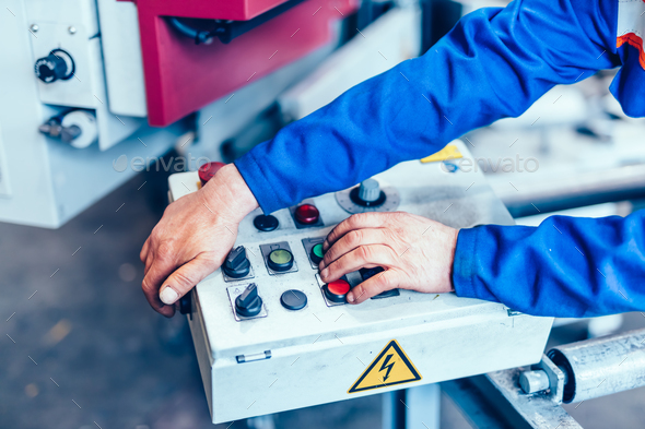 Worker operating saw machine for cutting steel profiles in a factory ...