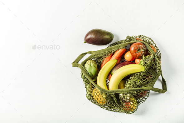 Fresh vegetables and fruits in a green string bag on a white background ...