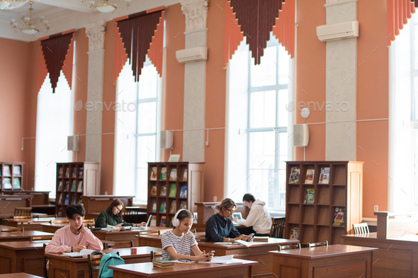Two rows of desks in college library and students working individually ...
