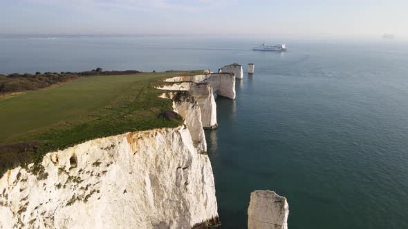 Aerial forward over white and jagged cliffs of Old Harry Rocks and ship ...