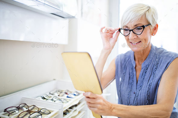 Beautiful mature woman choosing new pair of spectacles in opticians ...
