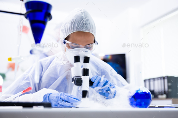 The researcher looks under the microscope near a beaker from which ...
