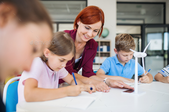 A group of small school kids with teacher in class learning about ...