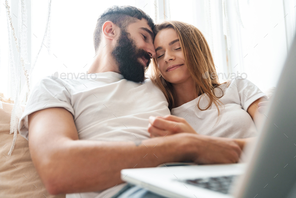 Image of romantic calm couple using laptop and hugging while sitting ...