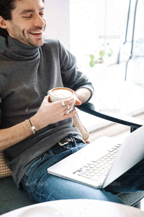 Image of young man working on laptop computer and drinking coffee in ...