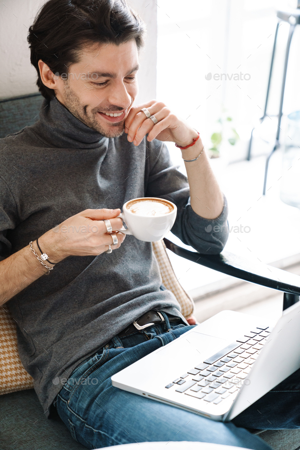 Image of young man working on laptop computer and drinking coffee in ...