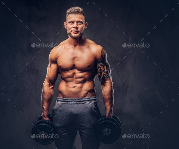 Handsome shirtless tattooed bodybuilder wearing sports shorts, posing ...