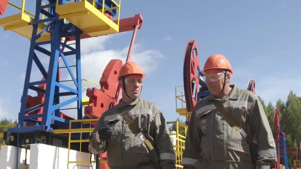Two Male Oil Workers Walking and Talking Near Oil Pump Jacks. Oil ...