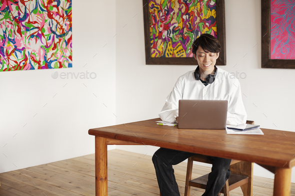 Japanese man siting at a table in an art gallery, looking at laptop ...